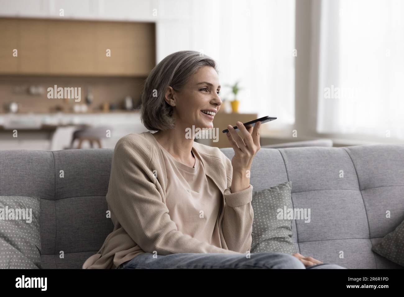 Cheerful dreamy mature woman making call on speaker phone Stock Photo ...