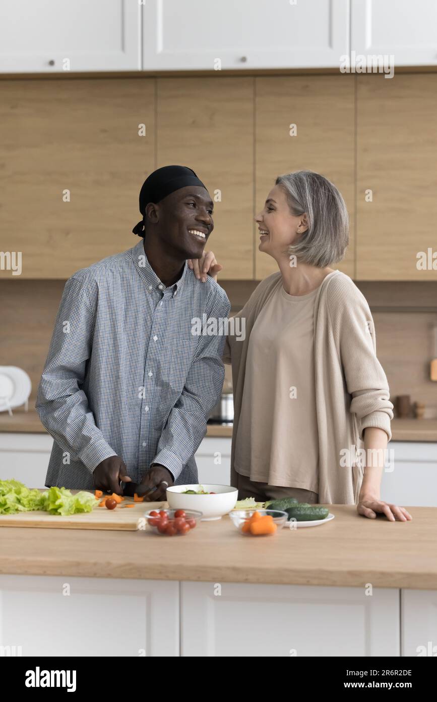 Joyful diverse couple of different ages and races cooking together ...
