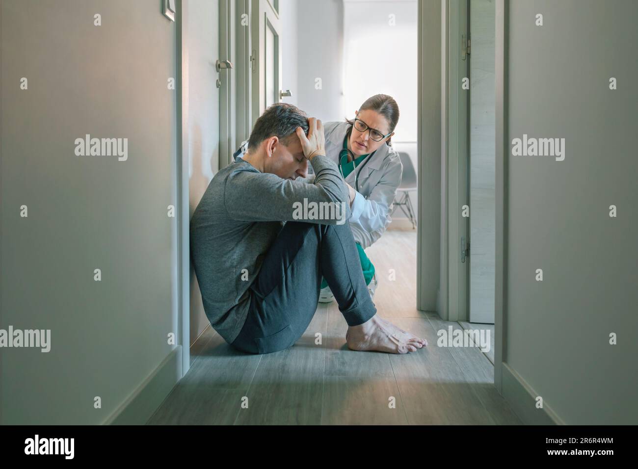 Psychiatrist reassuring and helping to patient sitting on room floor ...