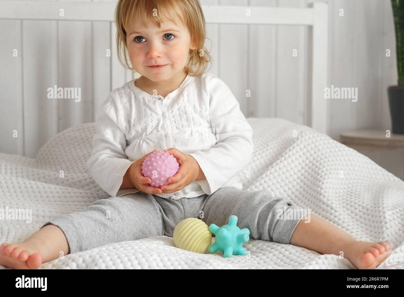 Cute baby girl playing tactile knobby balls. Young child hand plays ...