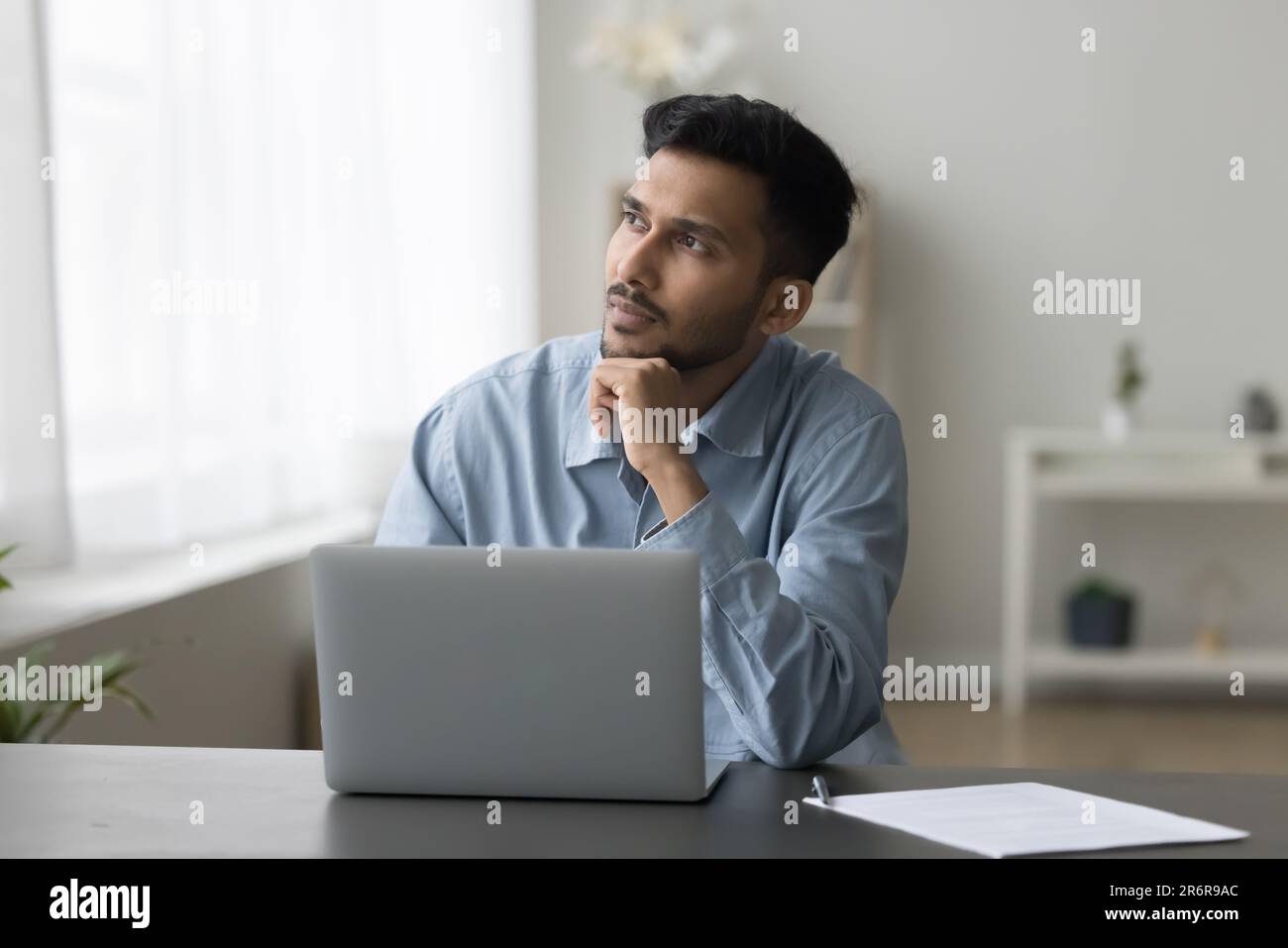 Serious attractive young Indian employee man thinking on business ...
