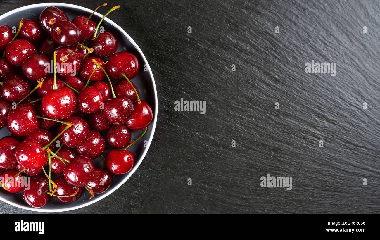 Fresh red ripe sweet cherry on plate on black slate, stone background ...