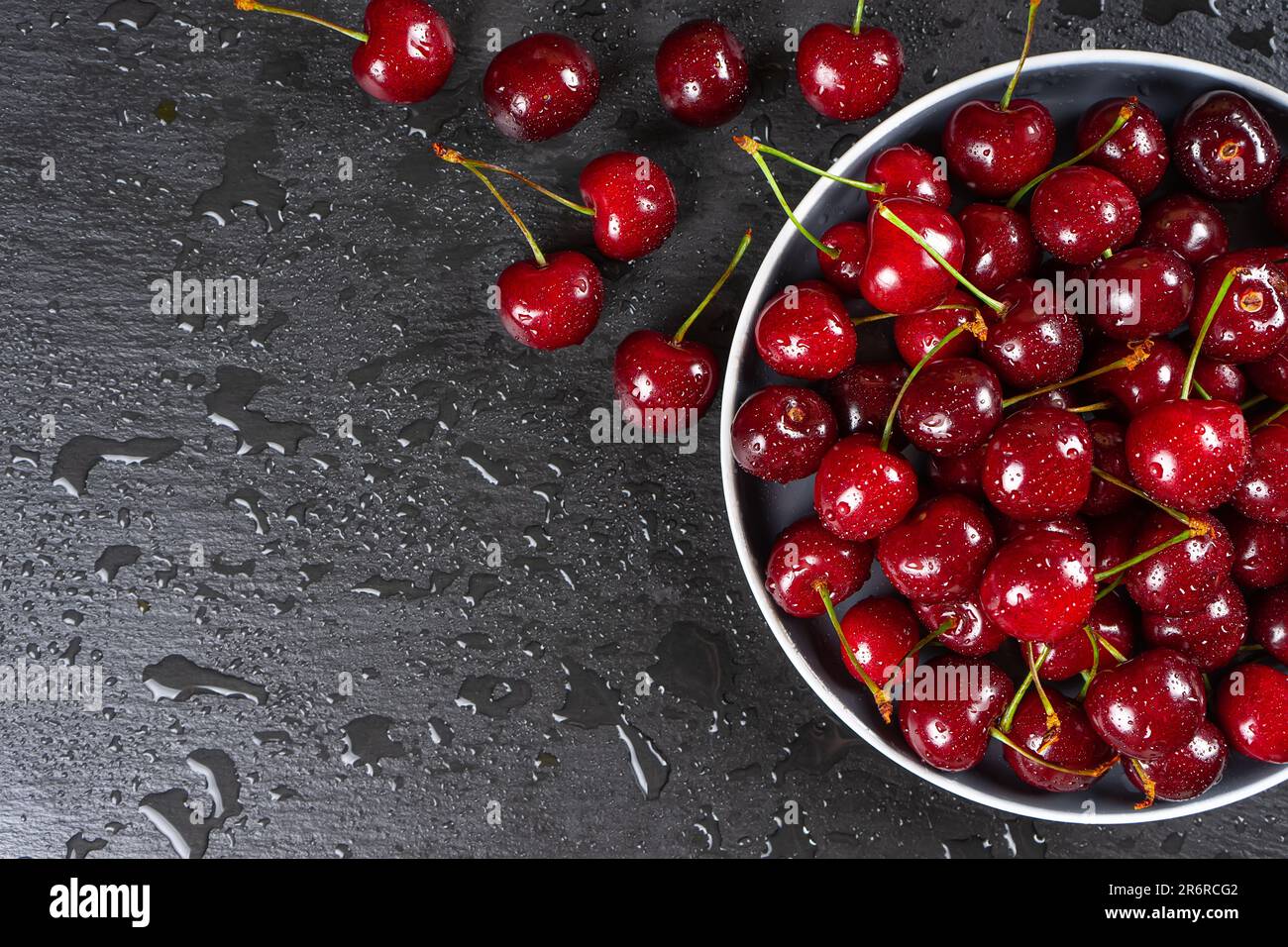Fresh red ripe sweet cherry with water drops on plate on black slate ...