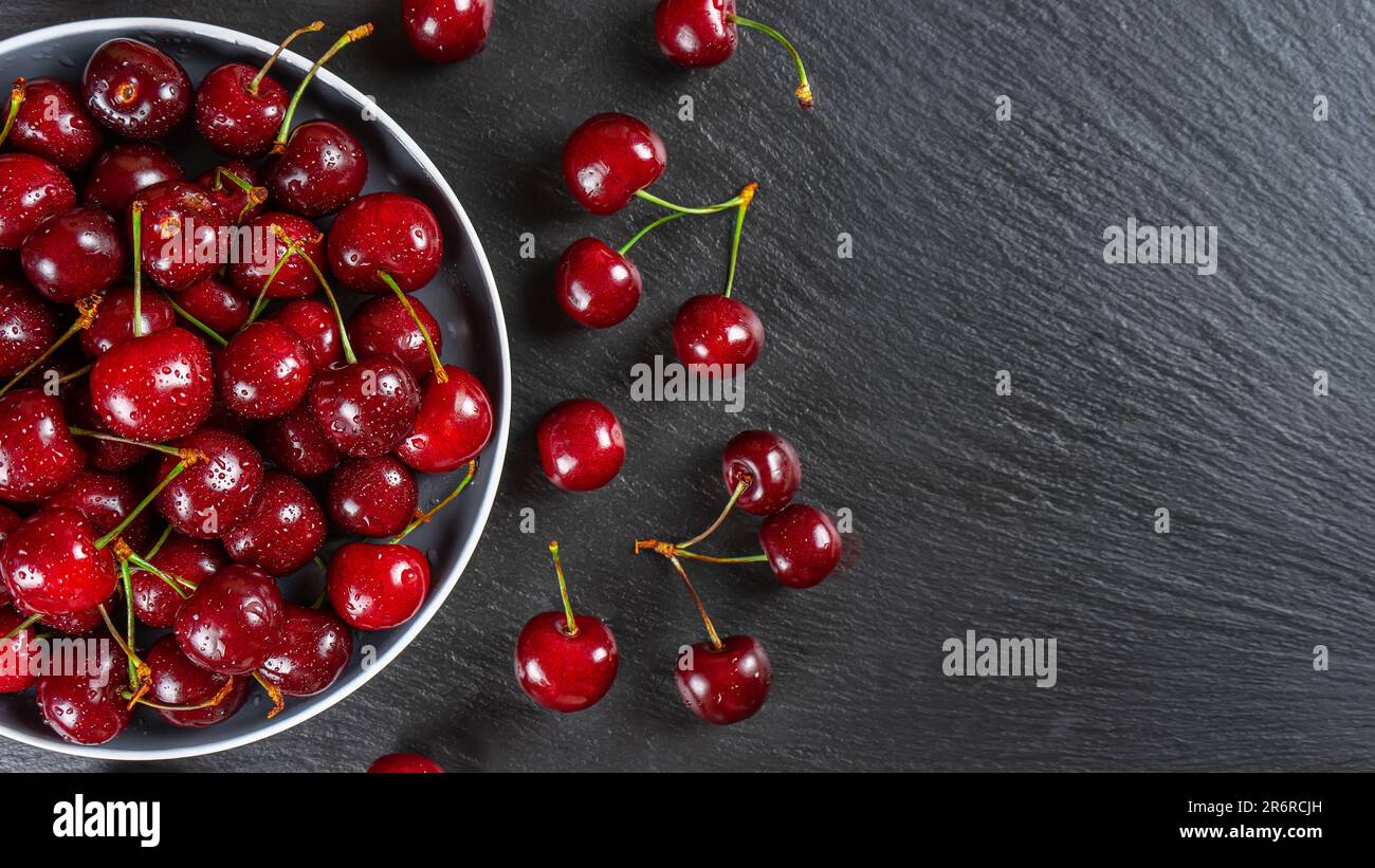Fresh red ripe sweet cherry with water drops on plate on black slate ...
