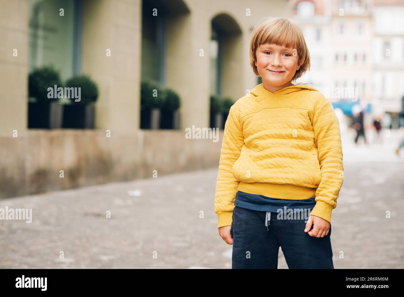 Outdoor portrait of handsome little boy in a city, wearing yellow hoody ...