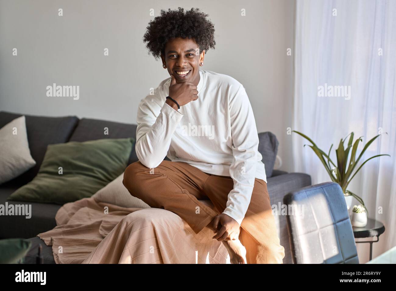 Young smiling gen z African American guy sitting on couch at home Stock ...