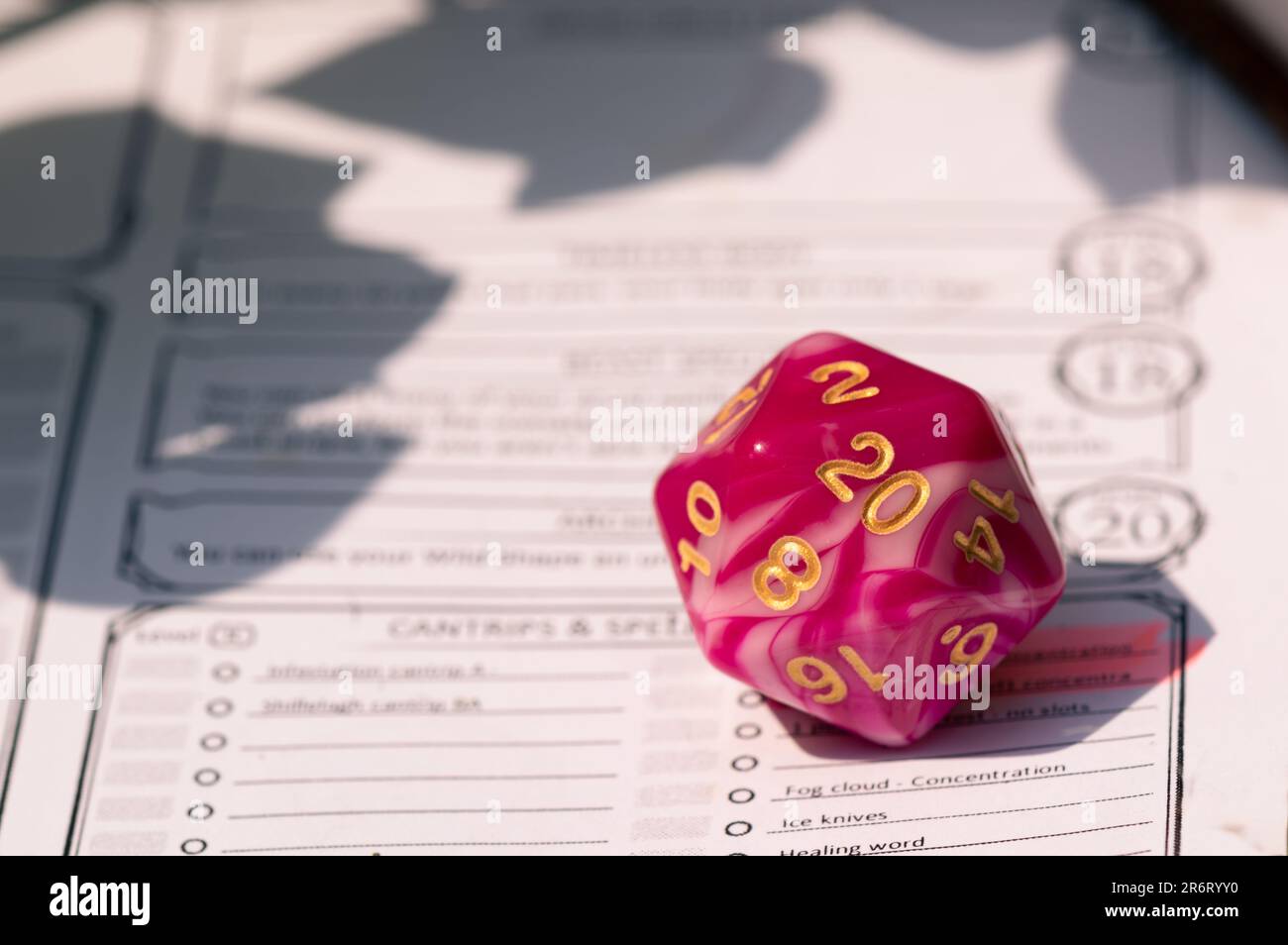 Close-up image of a pink role-playing gaming die on a character sheet ...