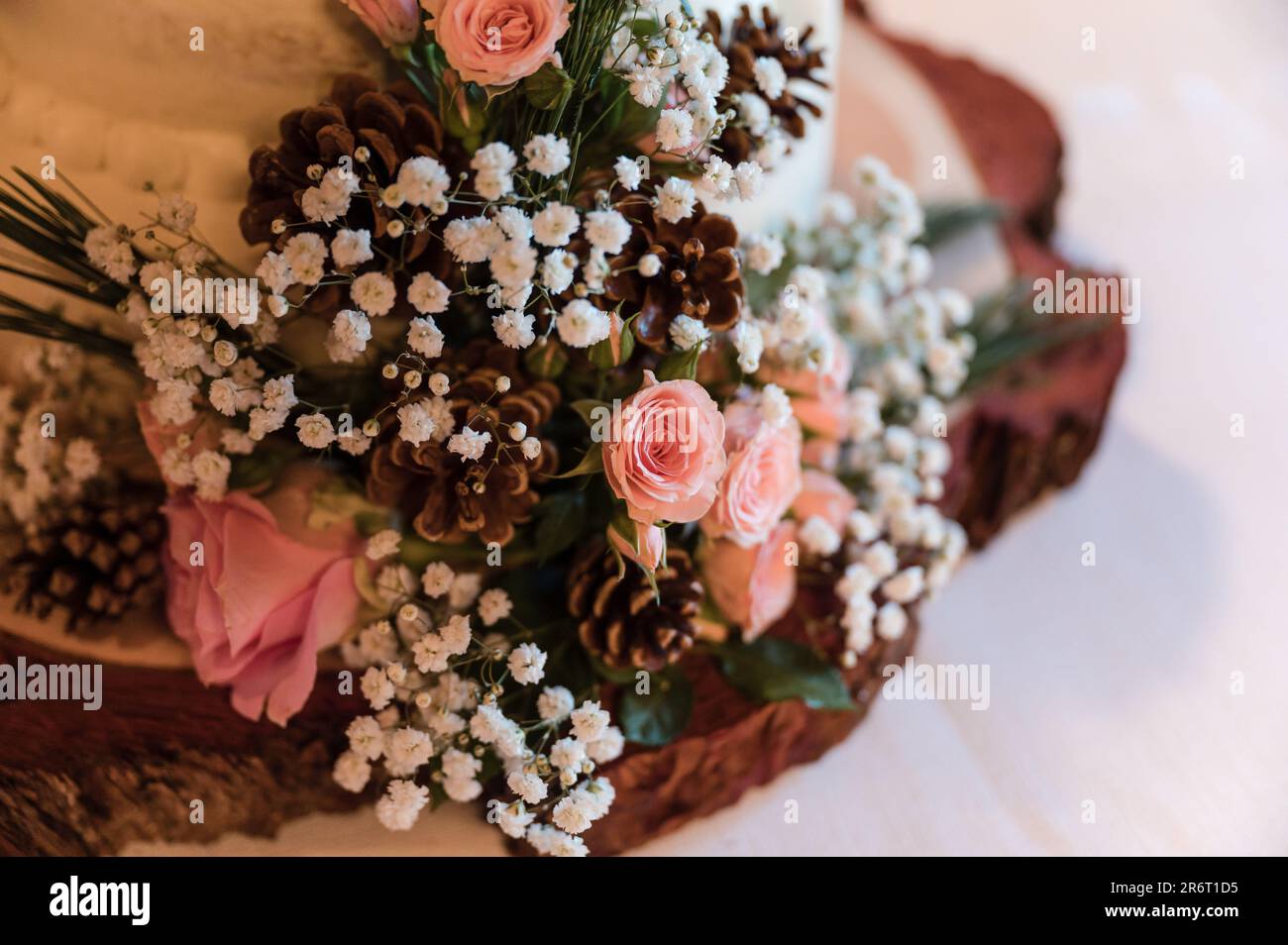 A three-tier white wedding cake adorned with pink roses, pine cones and ...