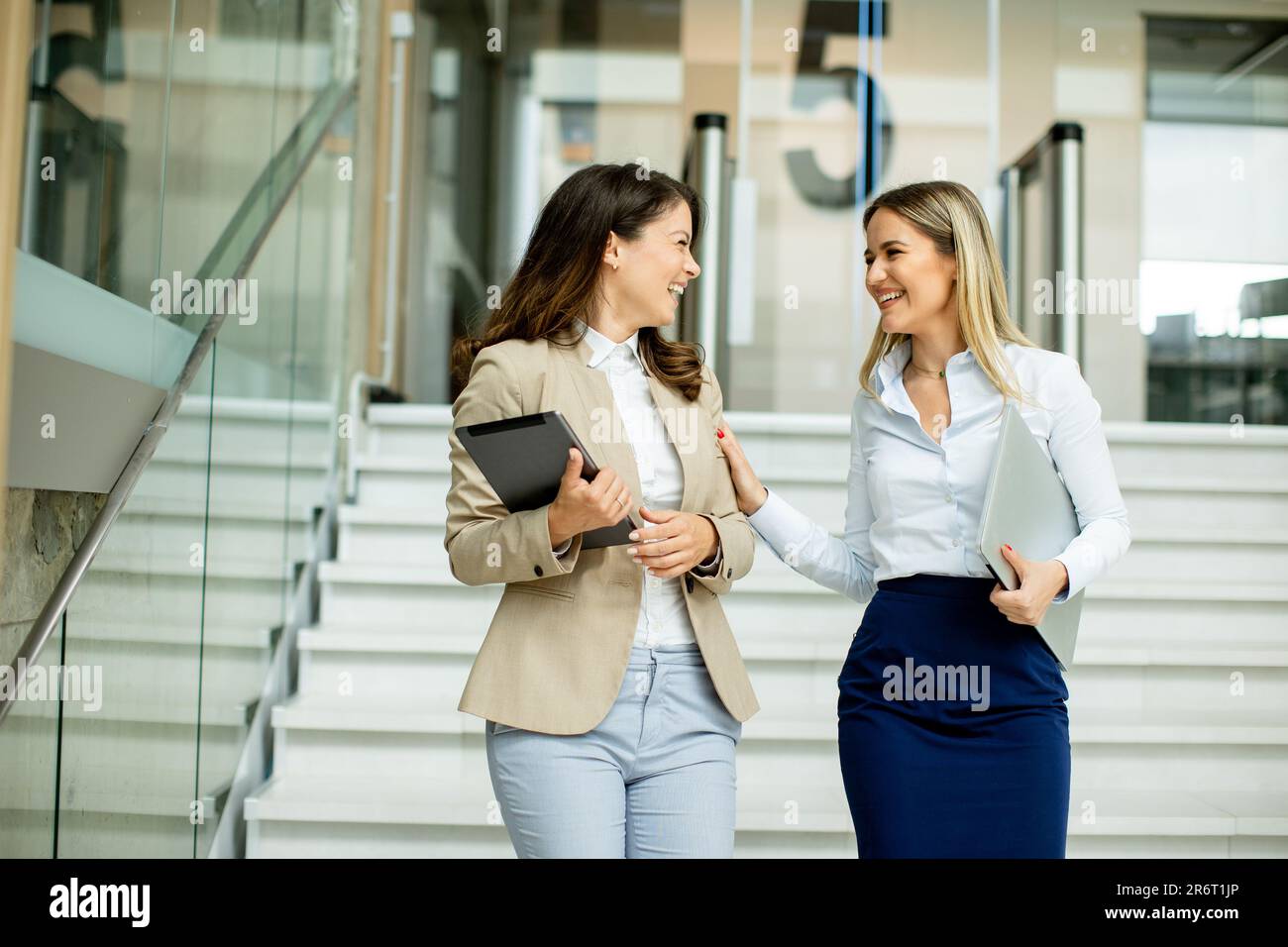 Two cute young business women walking on stairs in the office hallway ...