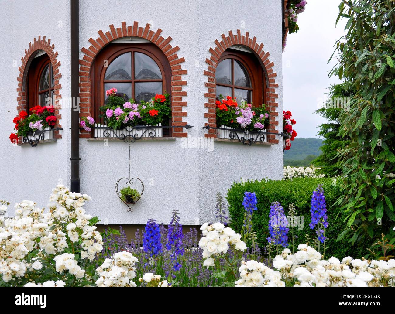 Garden with house, arched window with flowers, geraniums at the window ...