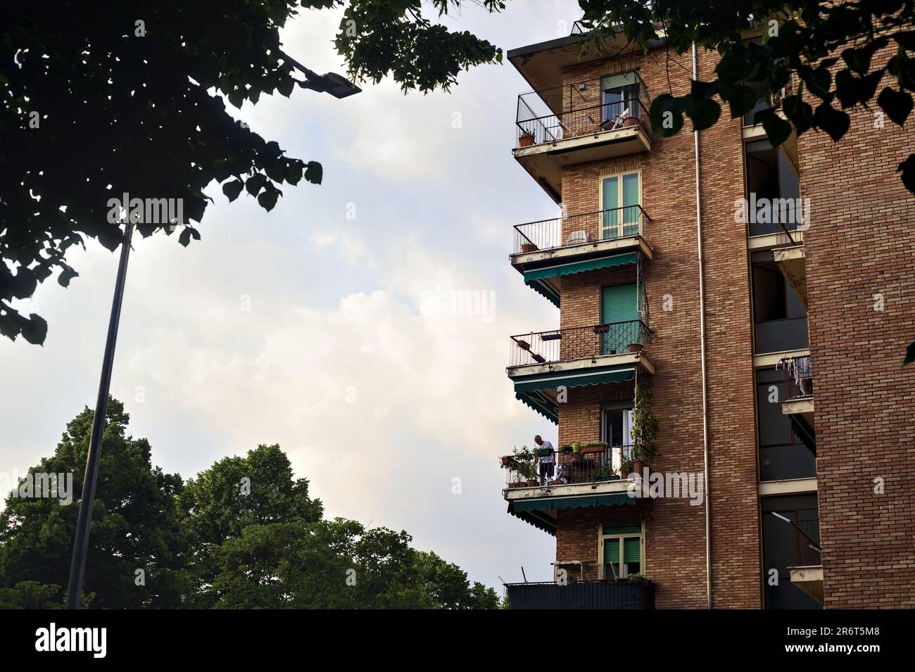 Facade and roof of a building next to trees with a cloudy sunset sky as ...