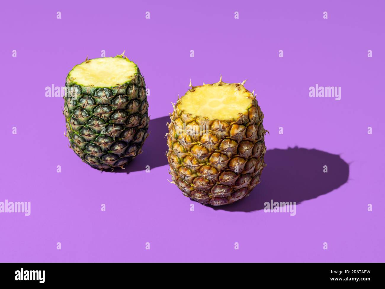 Two pineapple fruits with cut leaves minimalist on a purple-colored ...