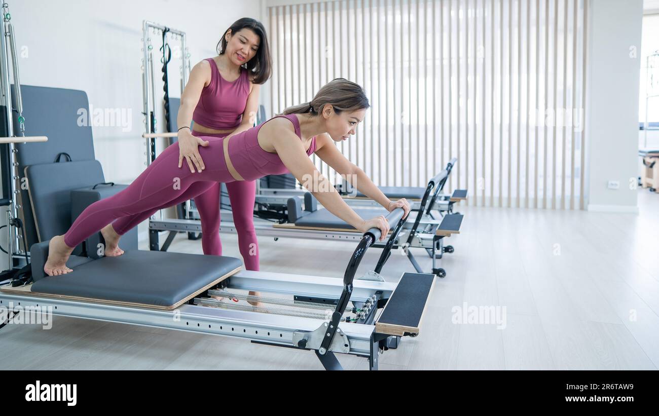 Asian woman doing plank on a reformer under the control of a trainer ...