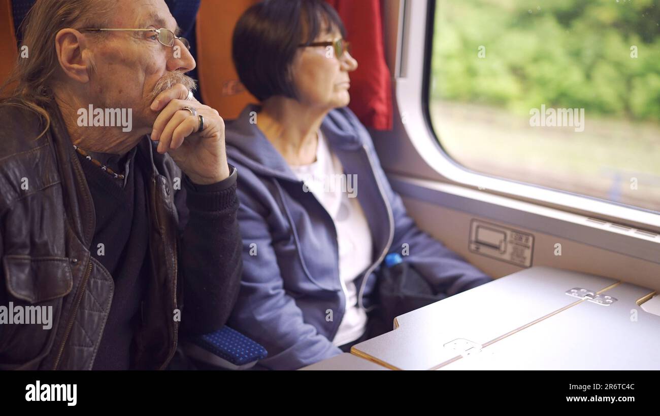 Elderly couple is riding in a train carriage and looking out the window ...
