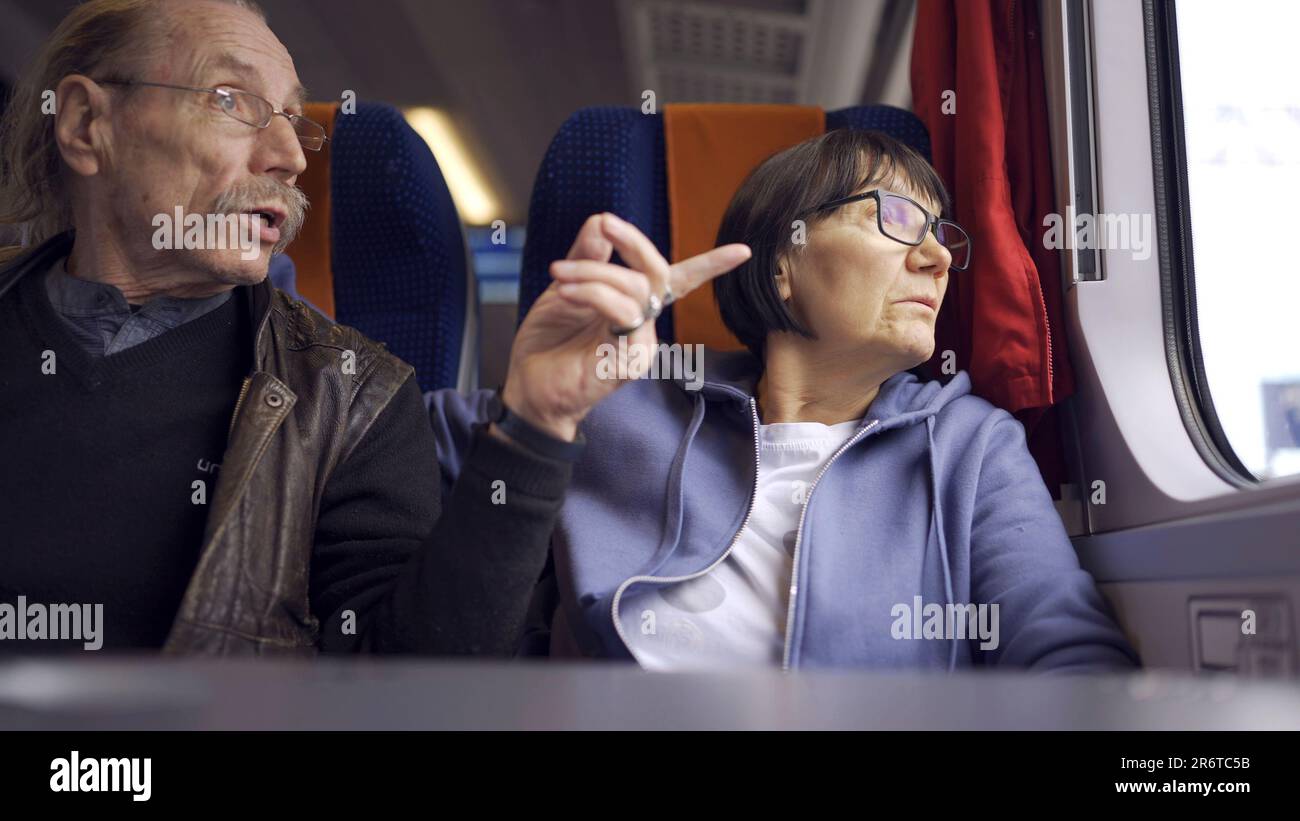 Elderly couple is riding in a train carriage and looking out the window ...