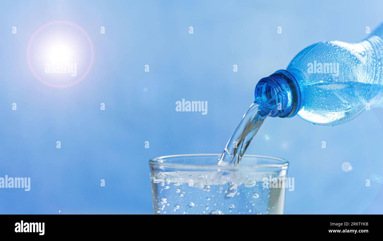 Fresh and cool water is poured from a bottle into a glass, against the ...