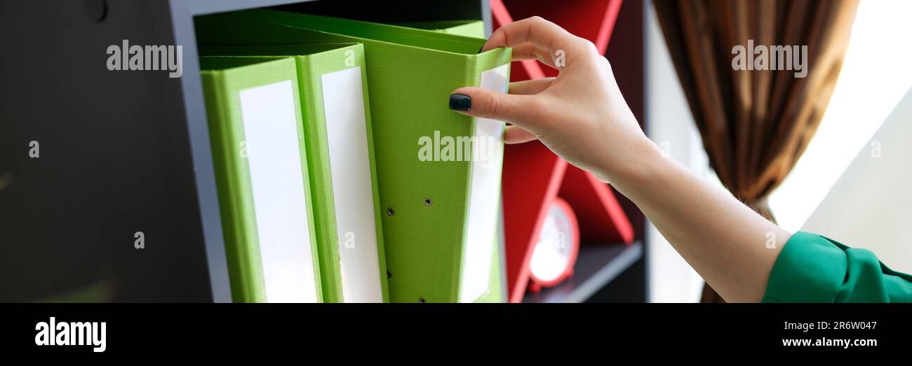 Woman taking off green folder with documents from shelf Stock Photo - Alamy