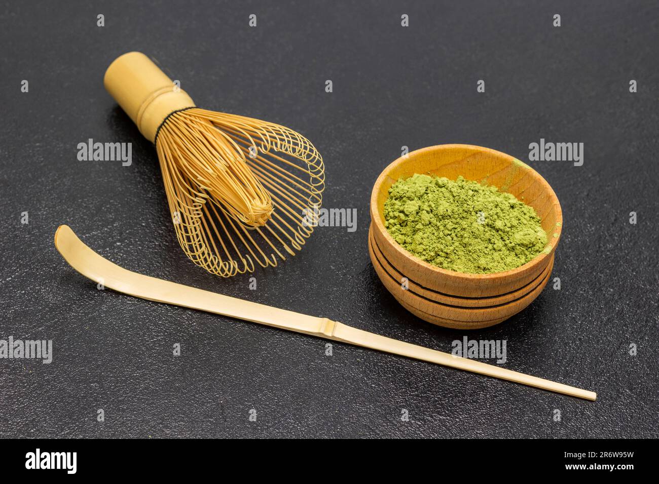 Matcha green tea powder in wood bowl. Bamboo whisk and measuring spoon ...