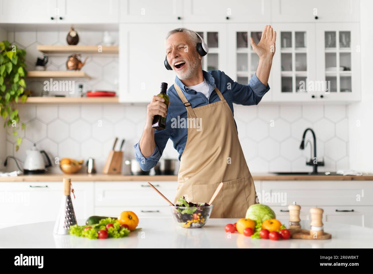 Cheerful Senior Man Having Fun While Cooking In Kitchen, Singing And ...