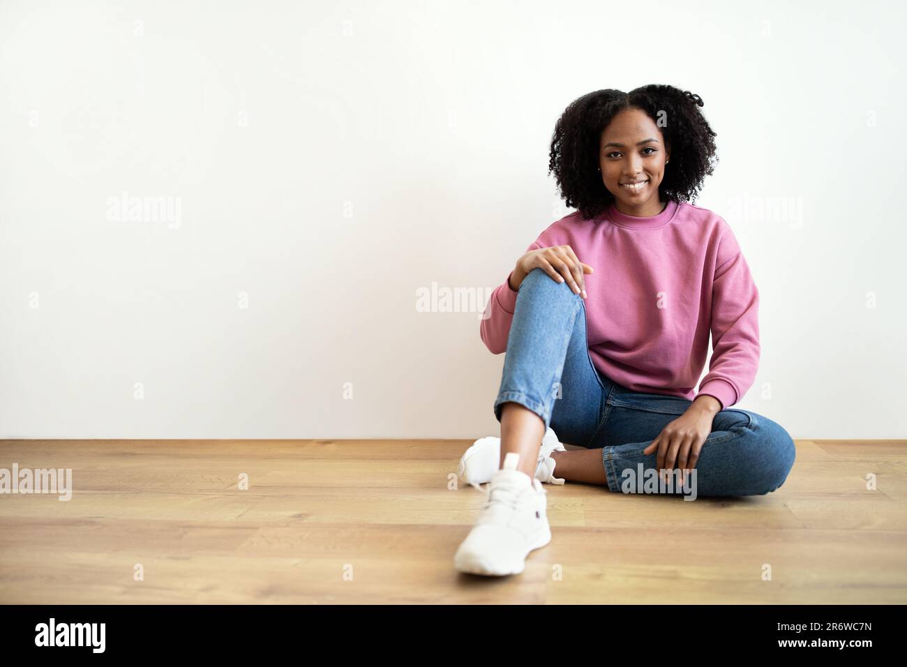 Happy millennial african american curly lady in casual sitting on floor ...