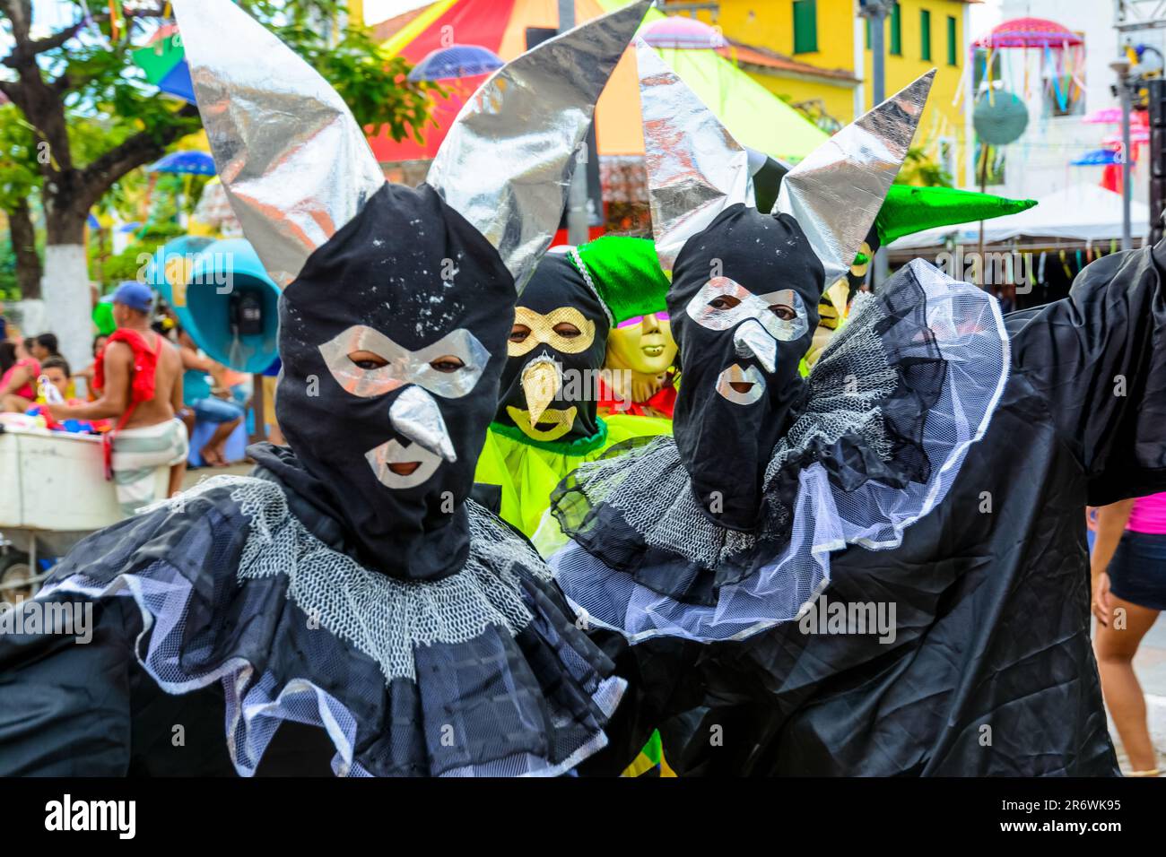 Masked people in costumes are lined up along a street in an outdoor ...