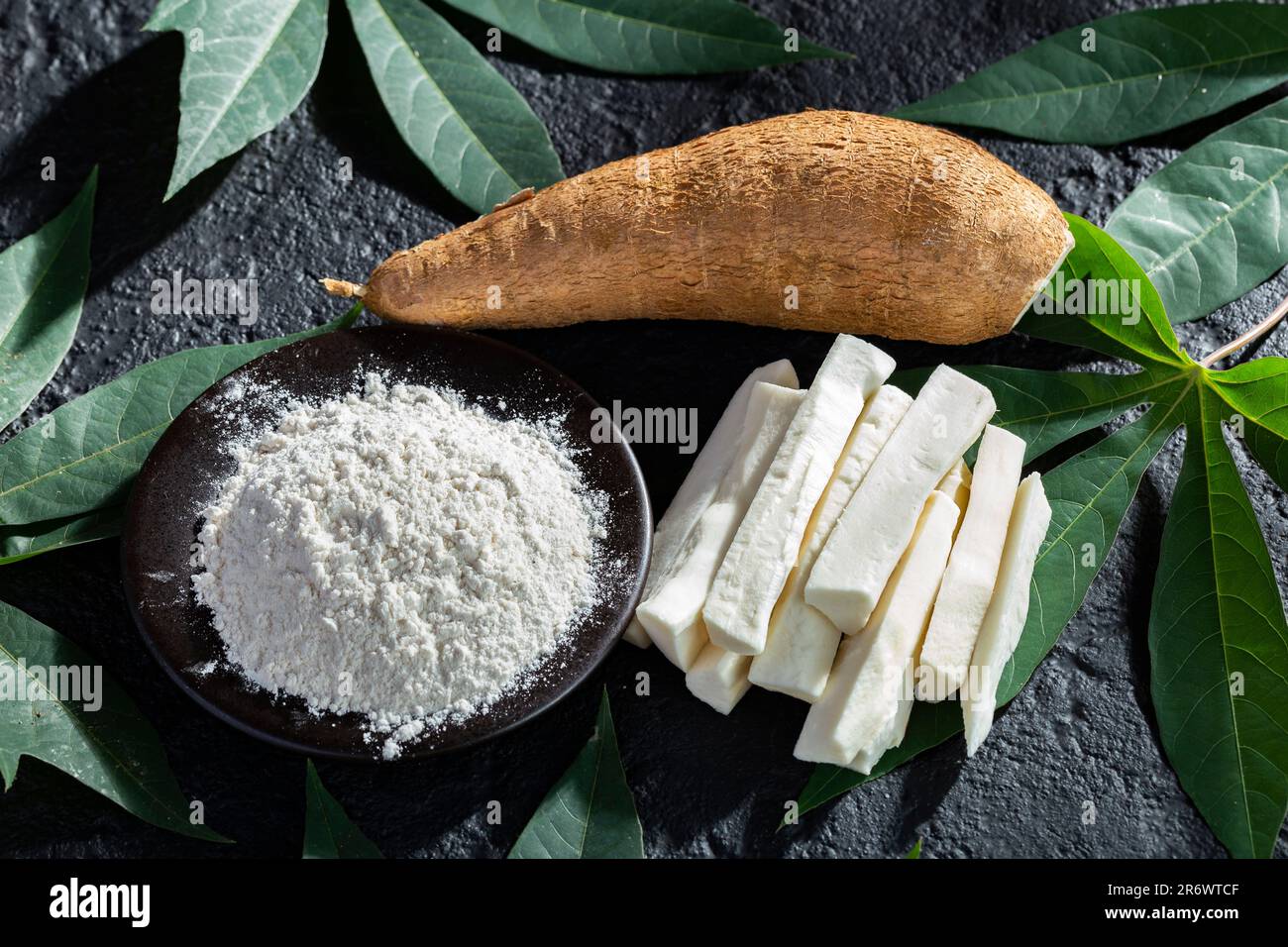 pile of cassava fruit and cassava flour on a background of rustic and dark texture (Manihot ...