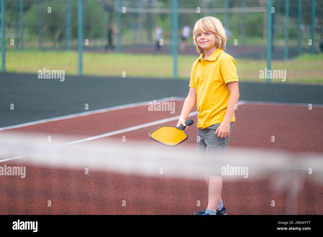 Happy blonde boy playing pickleball game, hitting pickleball yellow ...