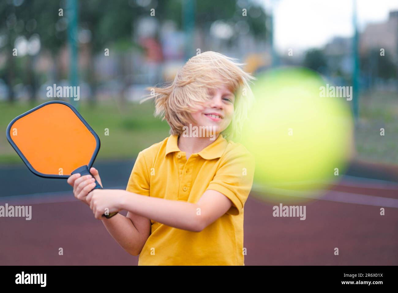Happy blonde boy playing pickleball game, hitting pickleball yellow ...