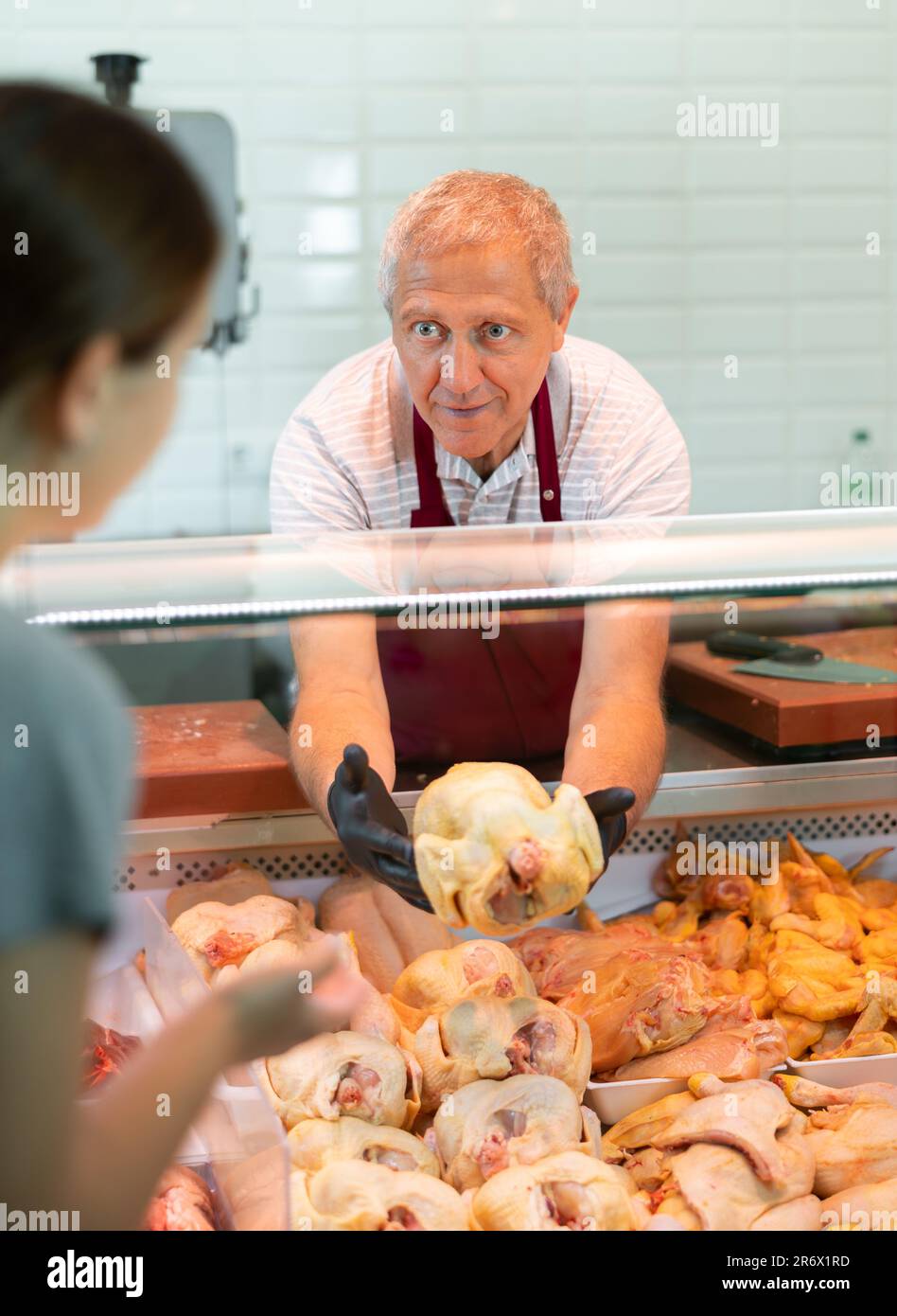 Elderly butchery shop owner offering chicken to female customer Stock ...