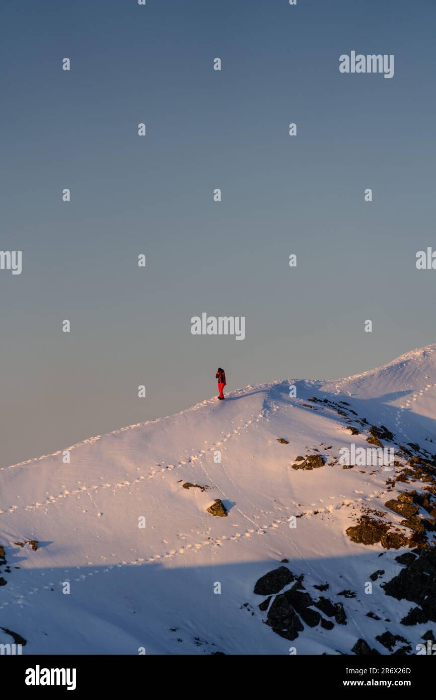 A lone individual stands atop a snowclad mountain, with a breathtaking ...