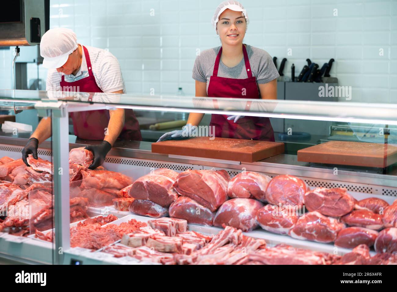 Adult man and young woman sellers lay out beef in butcher shop Stock ...