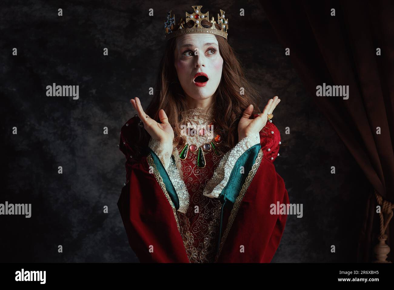 shocked medieval queen in red dress with white makeup and crown on dark ...