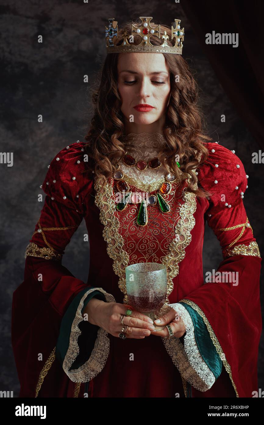 medieval queen in red dress with goblet and crown on dark gray ...