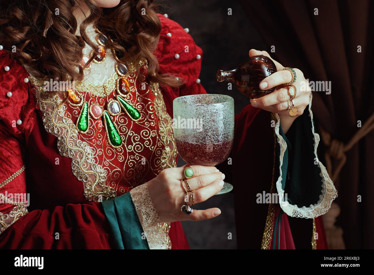 Closeup on medieval queen in red dress pouring poison into the goblet ...