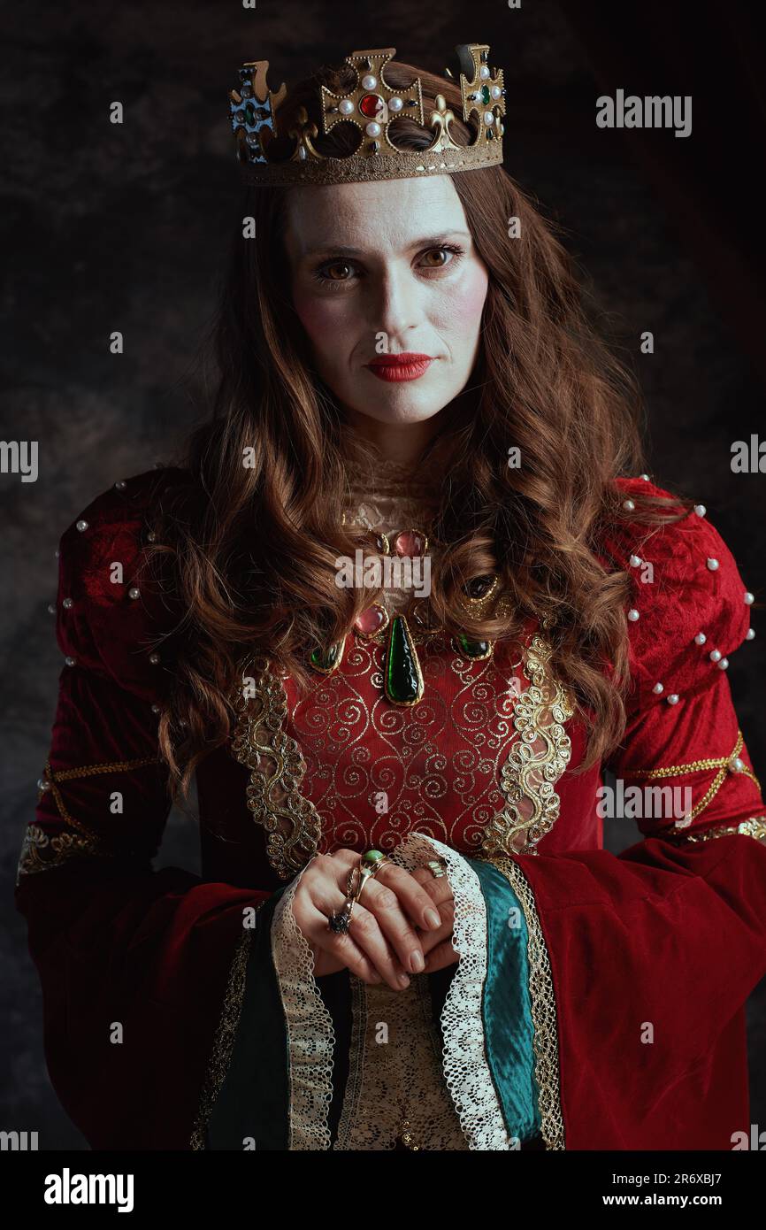 medieval queen in red dress with white makeup and crown on dark gray ...