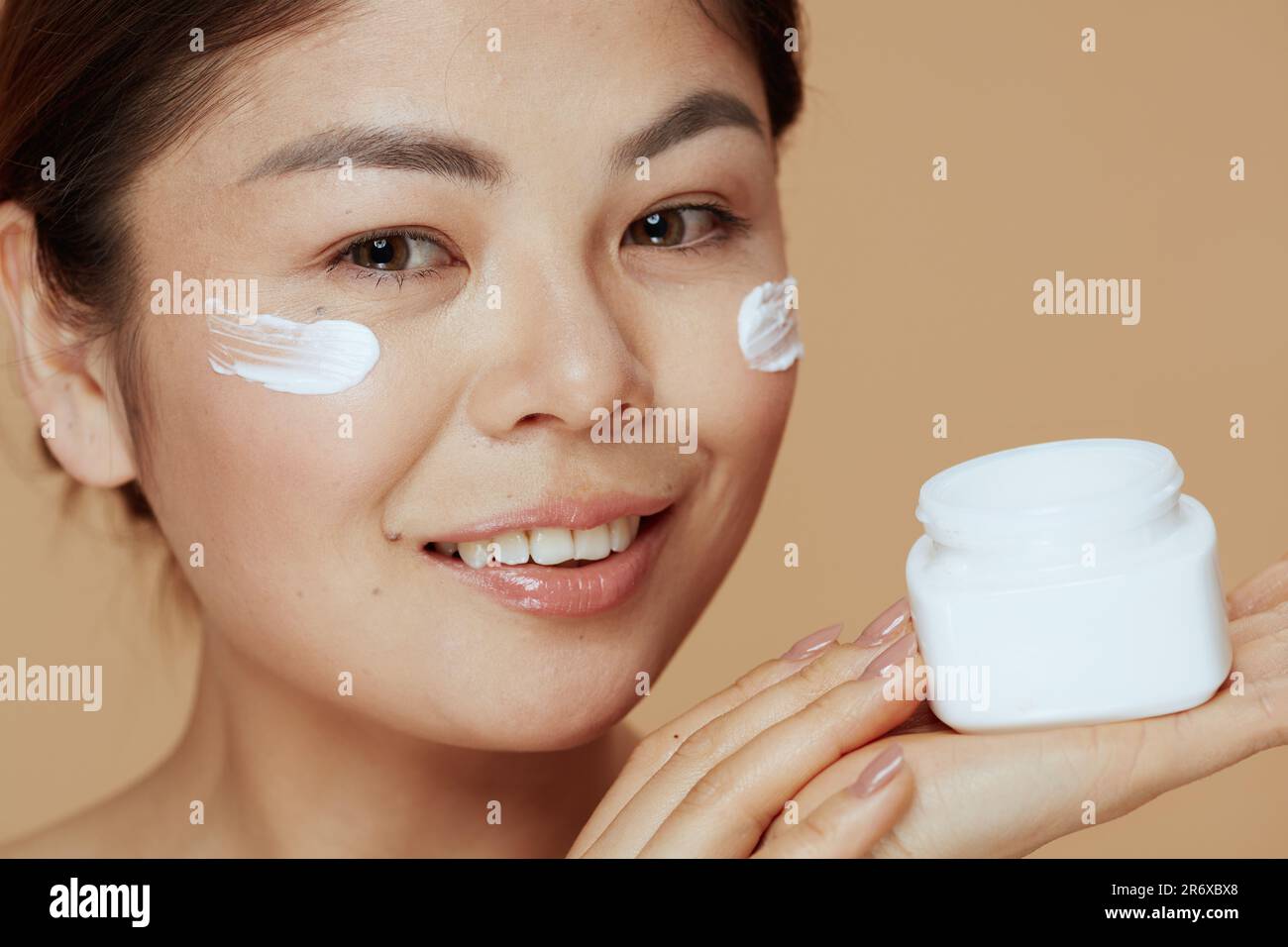 Portrait of modern asian female with facial cream jar and facial cream ...