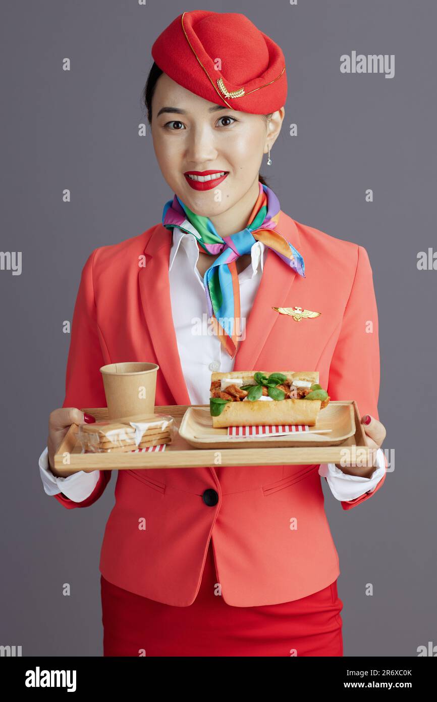 happy stylish asian female air hostess in red skirt, jacket and hat ...