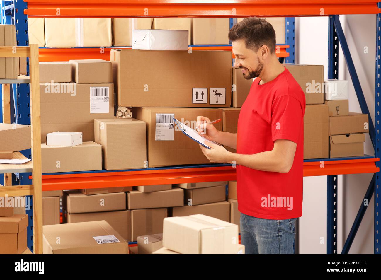 Post office worker with clipboard checking parcels at rack indoors ...