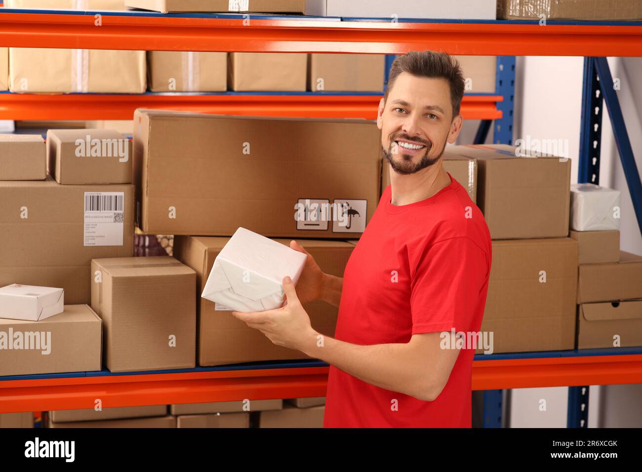Post office worker holding box near rack with parcels indoors Stock ...
