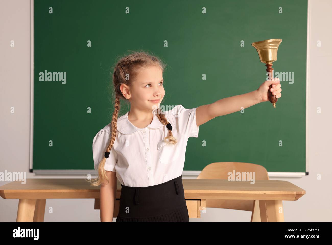Pupil with school bell near chalkboard in classroom Stock Photo - Alamy