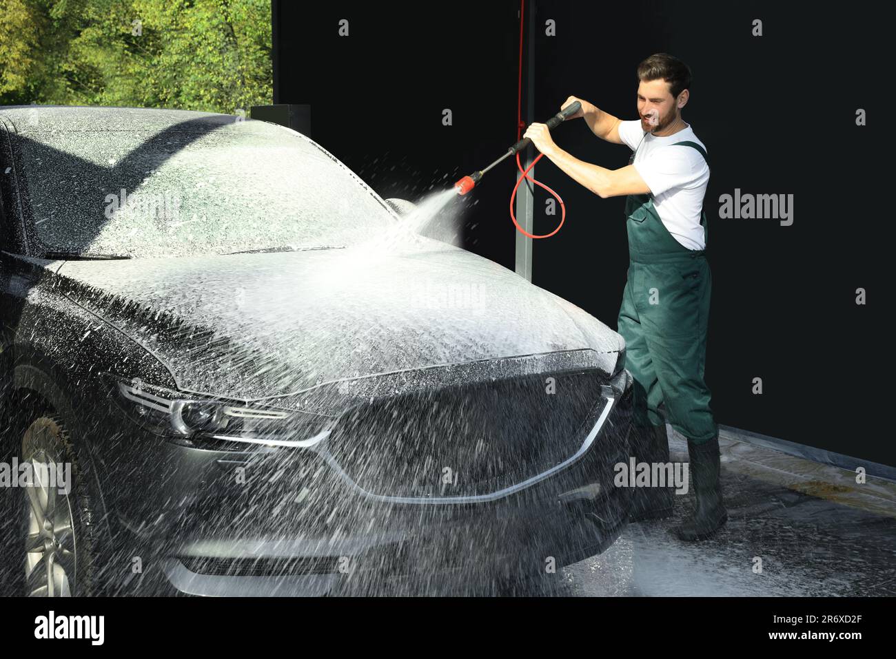 Worker washing auto with high pressure water jet at outdoor car wash ...