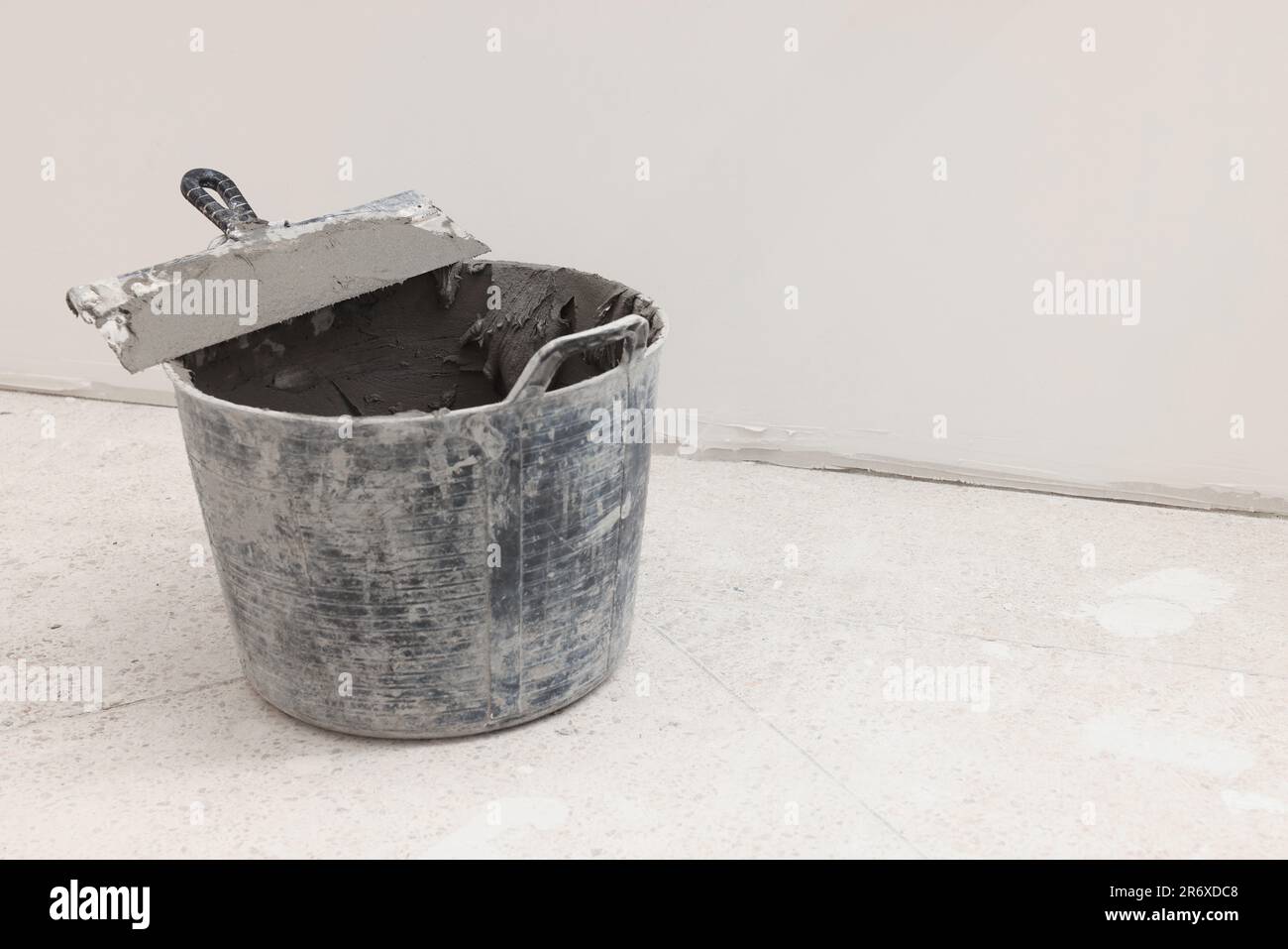 Bucket of adhesive mix and spatula on floor indoors, space for text ...