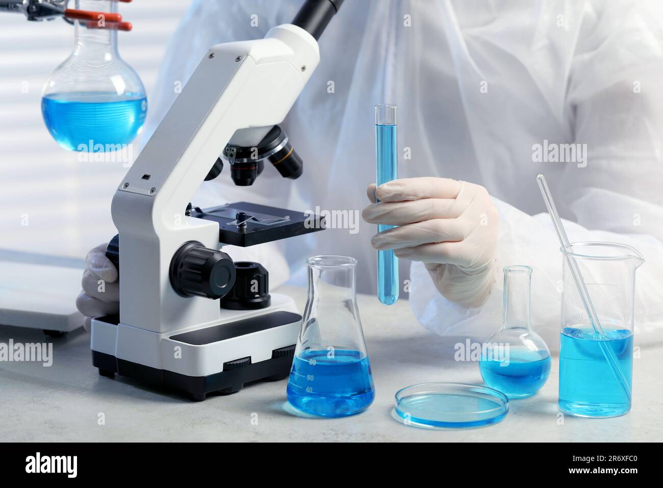 Scientist with test tube of light blue liquid near microscope in ...