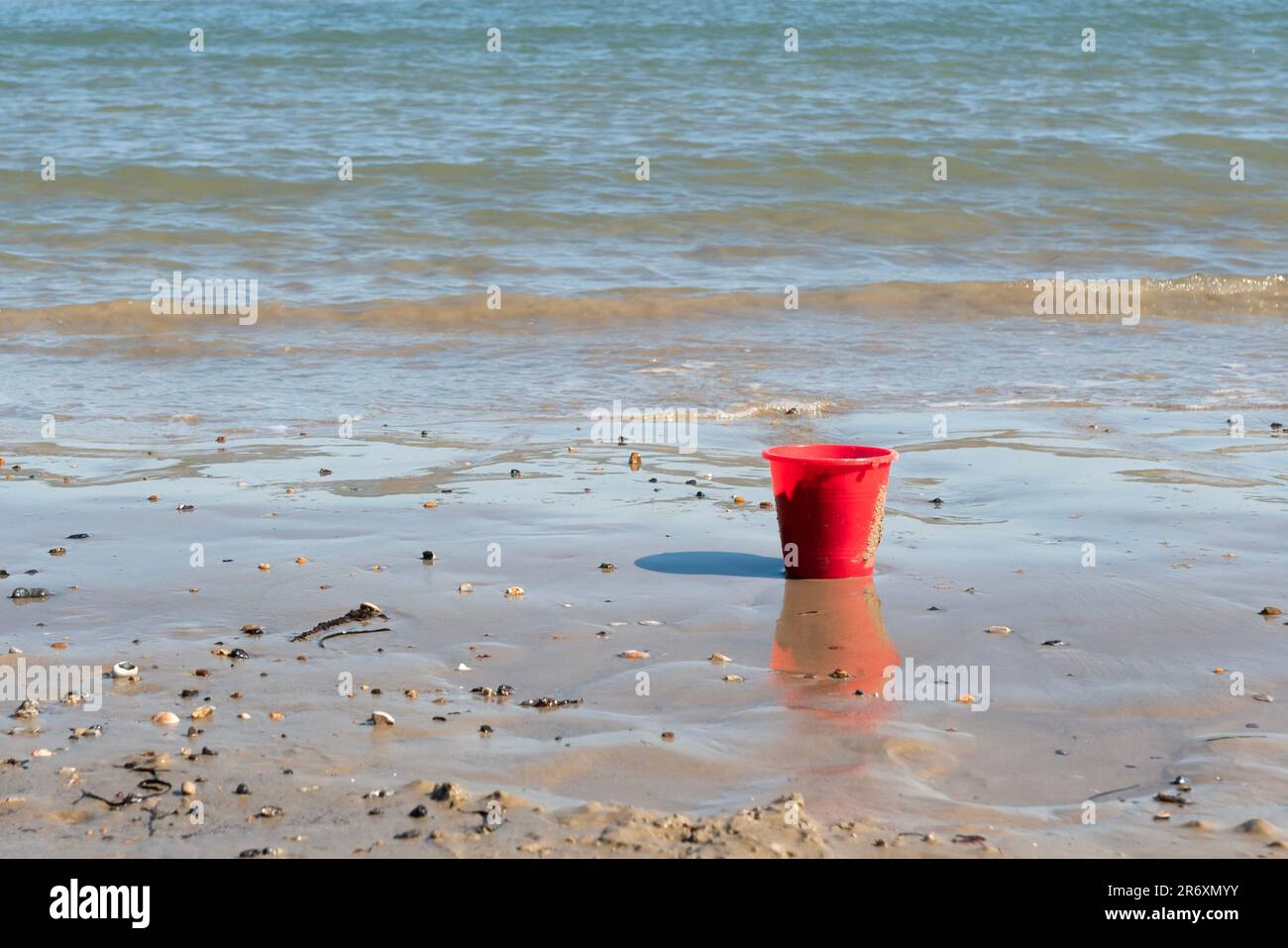 Red beach bucket forgotten on the shore Stock Photo - Alamy