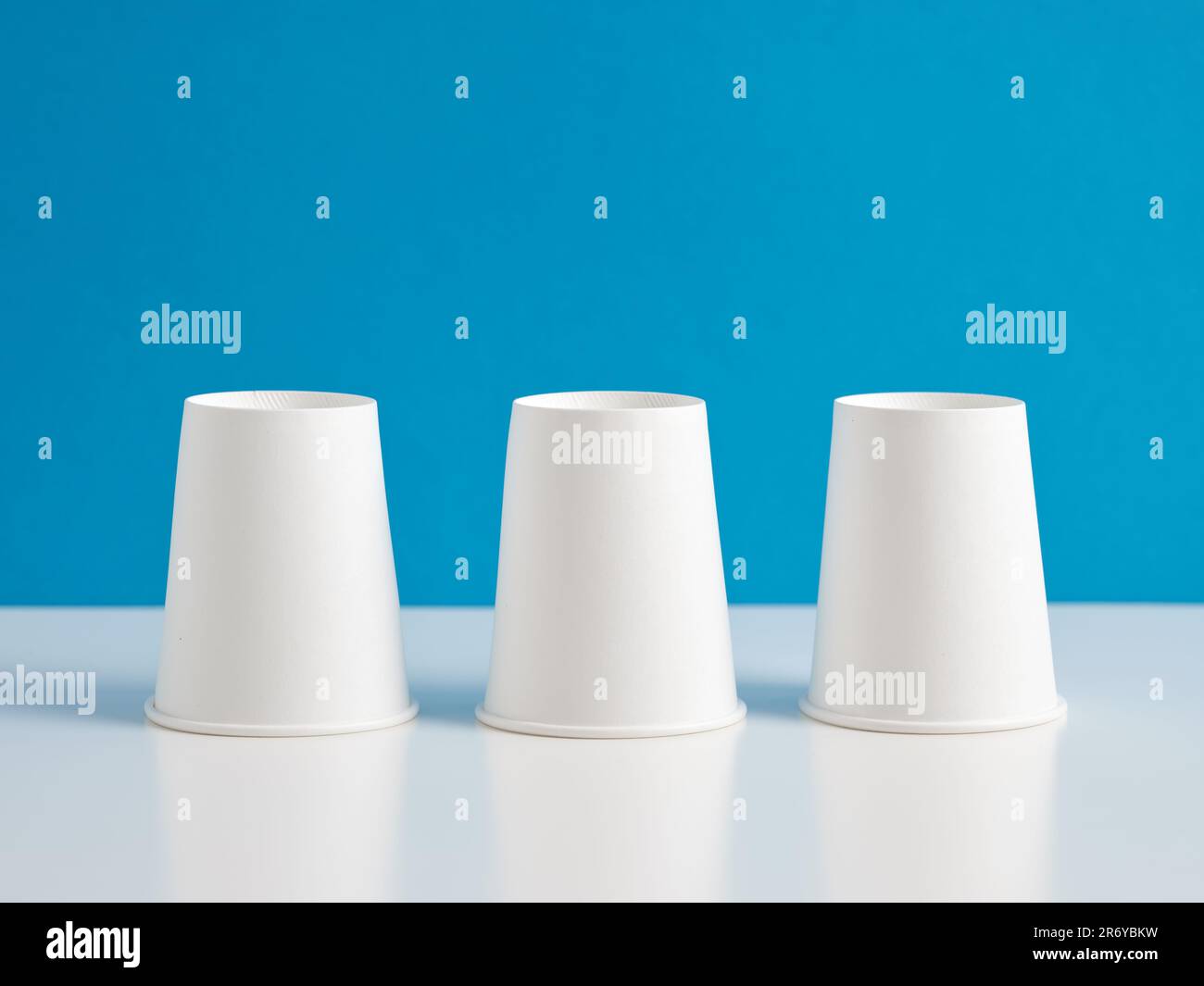 Three upside down flipped white paper cups on blue background Stock ...