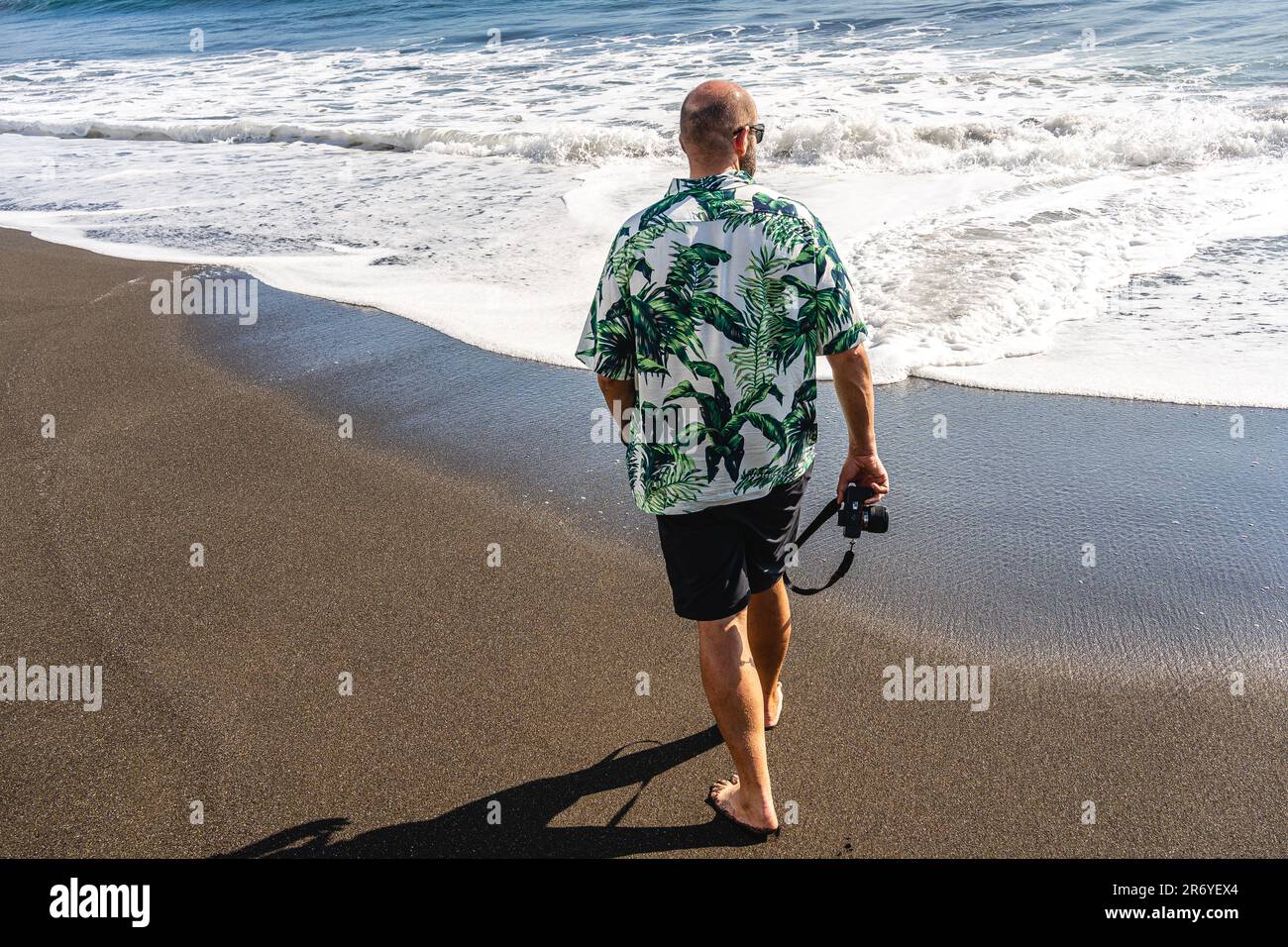 Rear view of a man with a camera walking along the beach Stock Photo ...