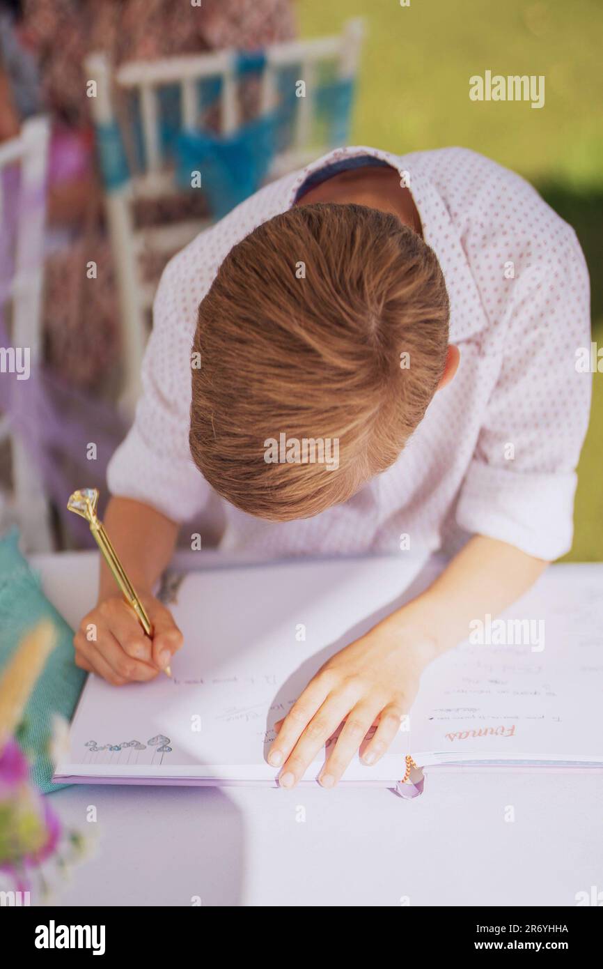 A vertical of a young boy seated at a desk, writing in a copybook Stock ...