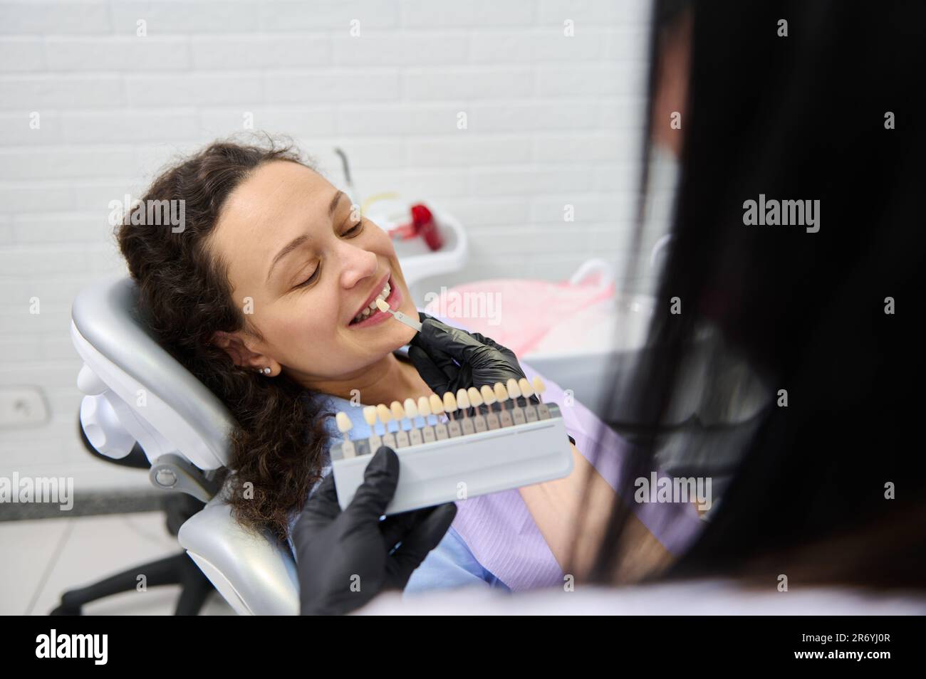 Dentist placing tooth color chart, over a smiling woman's teeth ...