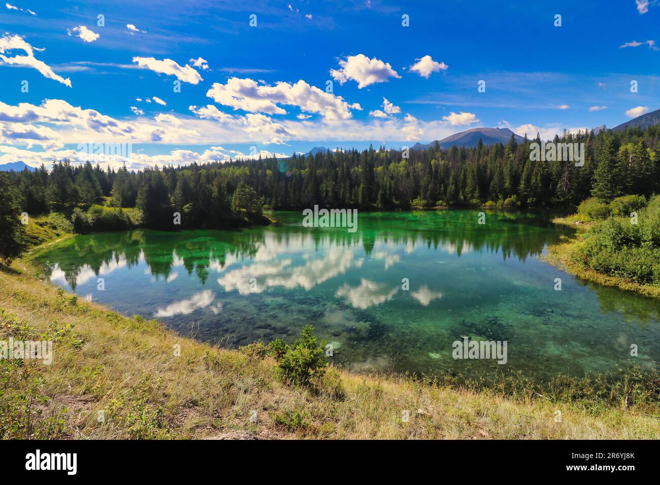Clouds scud across a bright blue sky and are reflected in the glassy ...