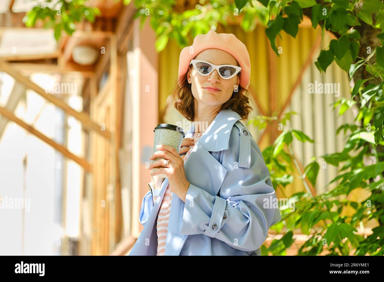 Stylish brunette woman in trendy trench coat enjoying tea in the old ...